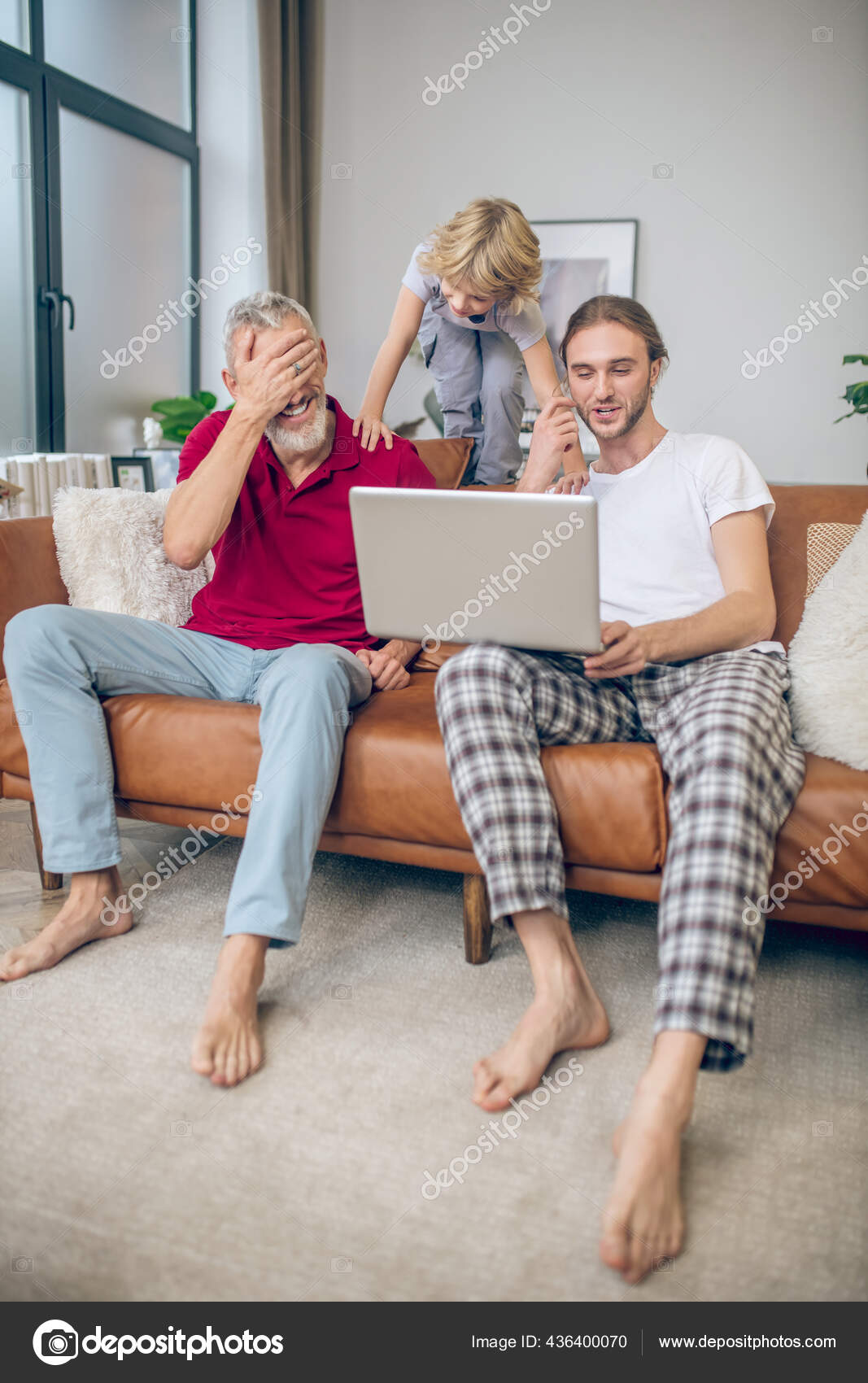 Two men and their son watching something on a laptop and having fun ...