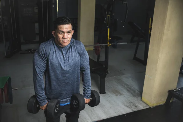 A buff asian guy does dumbbell shrugs at the gym. Traps workout and ...