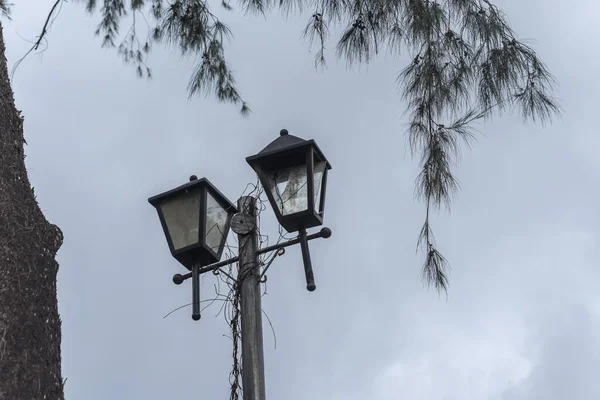 A broken, dilapidated old lamp post, in a highland area during overcast ...