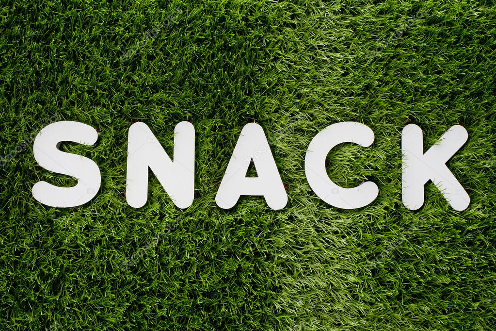 Word SNACK white wooden alphabet on gree grass background textur ...