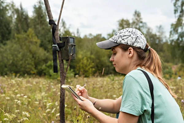 Young woman scientist zoologist writing down data from trap camera to ...