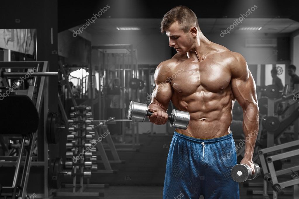 Muscular man working out in gym doing exercises with dumbbells at biceps, strong male naked ...