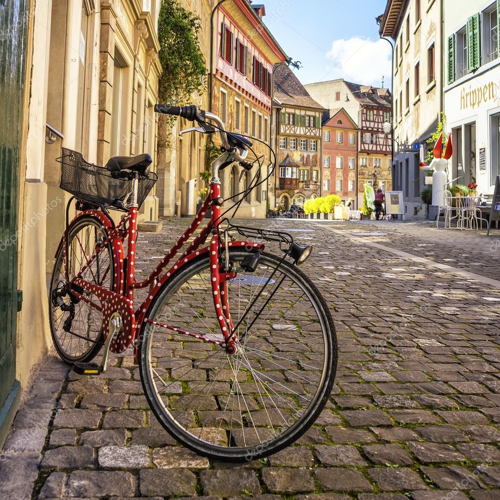 Red bicycle parked in street with ancient europe city in backgro ...