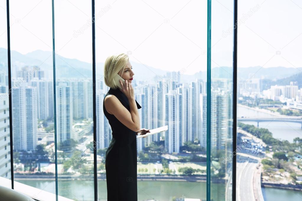 Young female CEO is calling via mobile phone, while is standing near ...