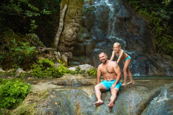 Father and daughter at a waterfall in the jungle. Traveling in nature ...
