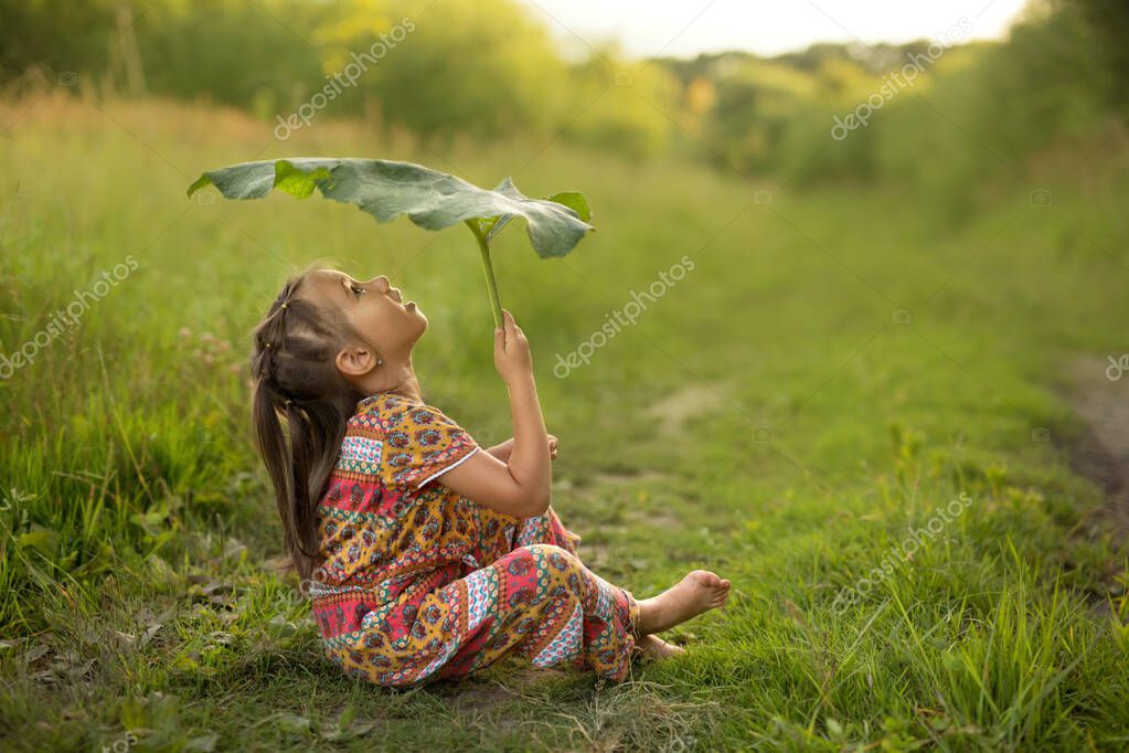 Una Niña Pequeña Se Sienta En El Césped Protegido De La Lluvia Por Una Gran Hoja De Bardana El