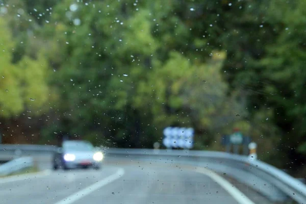 Blurred view through the windshield of a car while driving on a rainy day. Raindrops on the ...