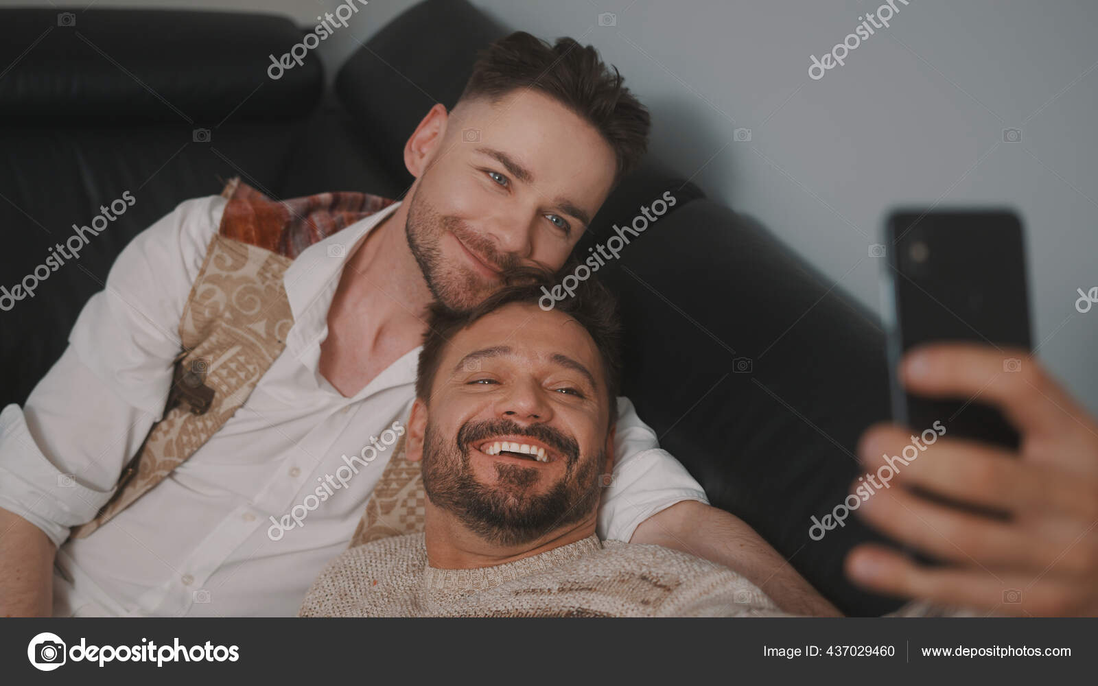 Male romantic gay couple relaxing on the couch. Boyfriend kissing his partner in the head ...