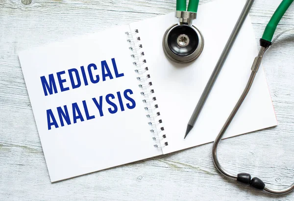 MEDICAL ANALYSIS is written in a notebook on a light wooden table next ...
