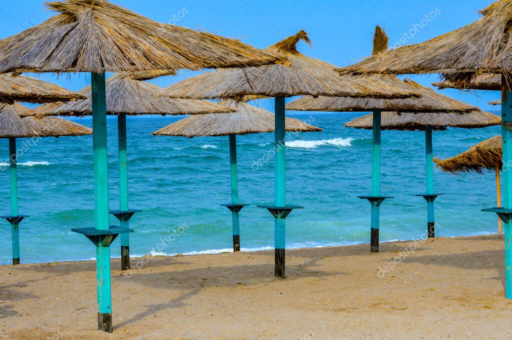 Sombrillas de playa de paja que proporcionan sombra en la costa arenosa ...