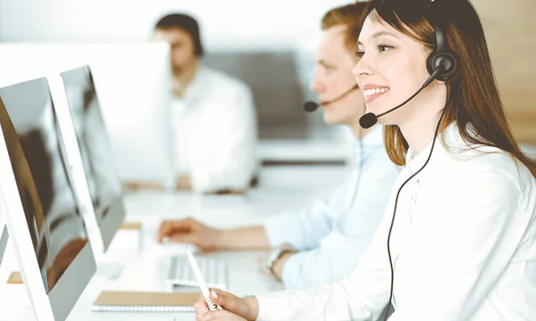 Group of diverse operators at work in call center. Beautiful asian woman sitting in headset at ...