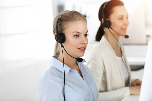 Blond woman working in sunny call center. Group of diverse people working as customer service ...