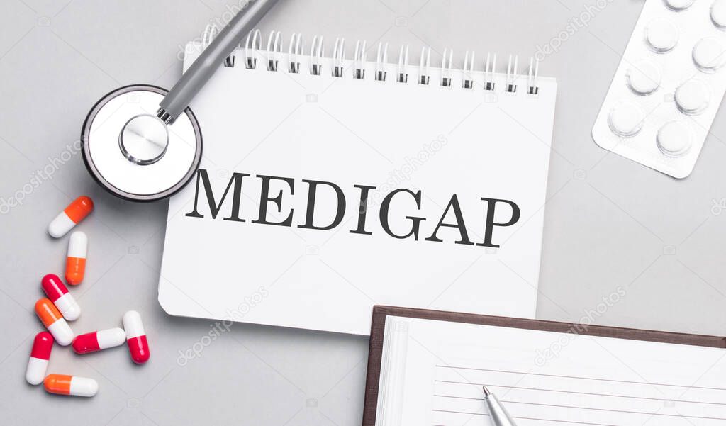 Estetoscopio, pastillas y cuaderno con texto medigap en la mesa médica ...