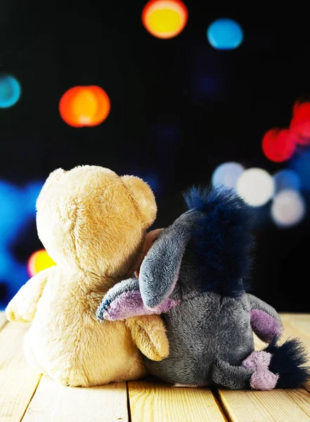Two teddy bears hugging their backs on a wooden table and defocused lights background. Tender ...
