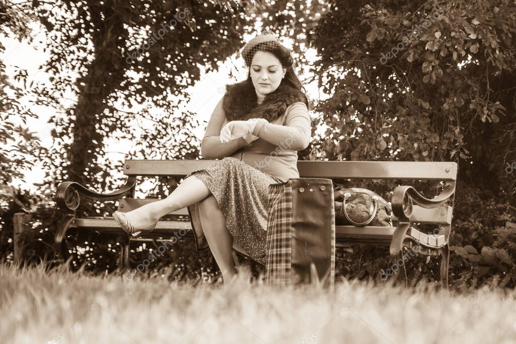 Hermosa joven posando en ropa vintage de la década de 1940, esperando en un banco en un parque 2022
