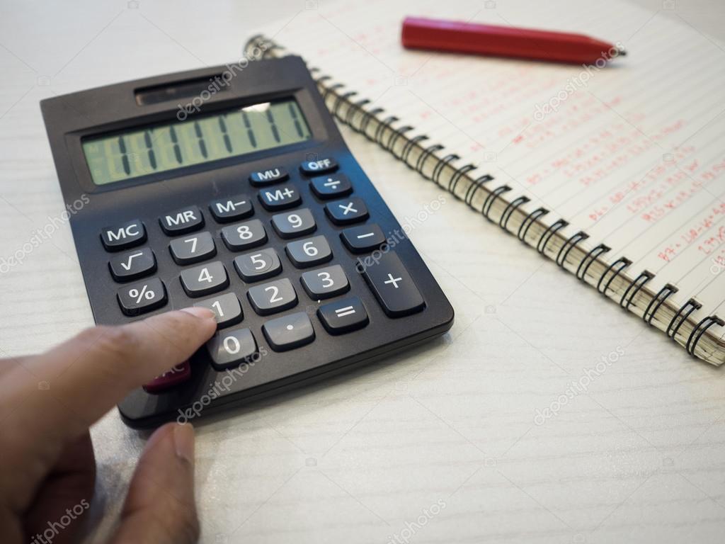 Calculadora, una mano, cuaderno y lápiz sobre mesa de madera. 2023