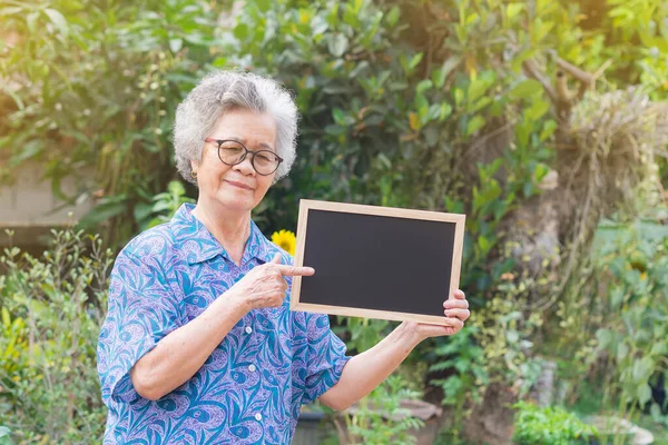 A portrait of an elderly woman point to a blackboard while standing in ...