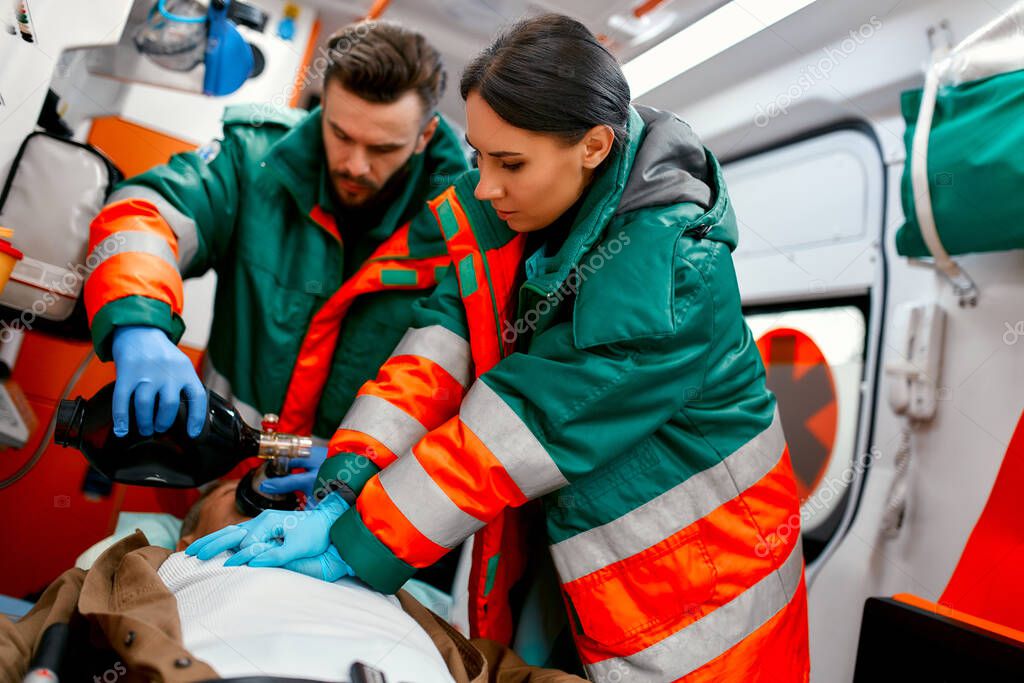 Dos paramédicos están resucitando a un anciano acostado en una camilla ...