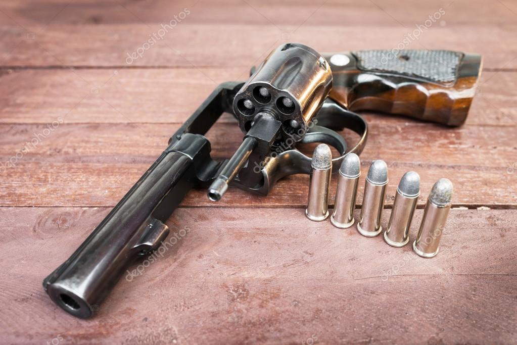 revólver negro con balas aisladas sobre fondo de madera 2024