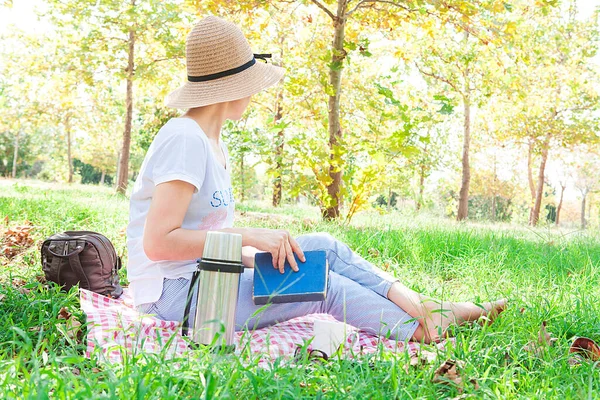 Young woman with book in hands is having a picnic in the countryside ...