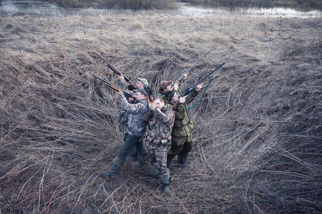 Group of hunters standing back to back in rural field and aiming and ...