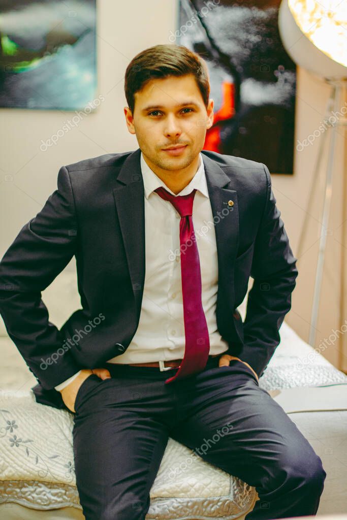Hombre de traje y corbata roja sentado en el borde de la cama. Hombre de traje en la habitación ...