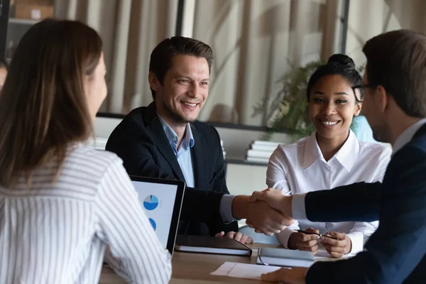 Smiling diverse business partners shaking hands at group negotiations ...