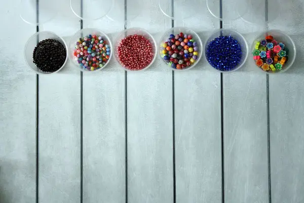 Multicolored beads in round plastic boxes on a wooden background ...