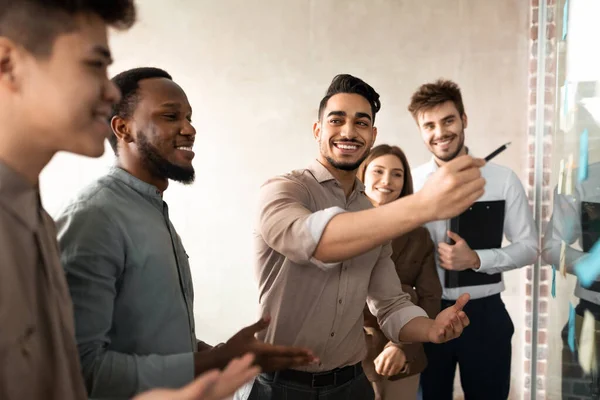 Colleagues having meeting using sticky post-it notes on glass wall ...