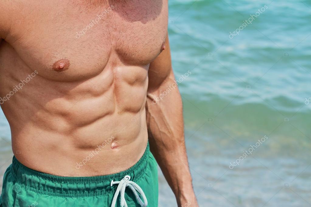 Hombre musculoso fuerte en la playa, cerca del estómago y el pecho ...