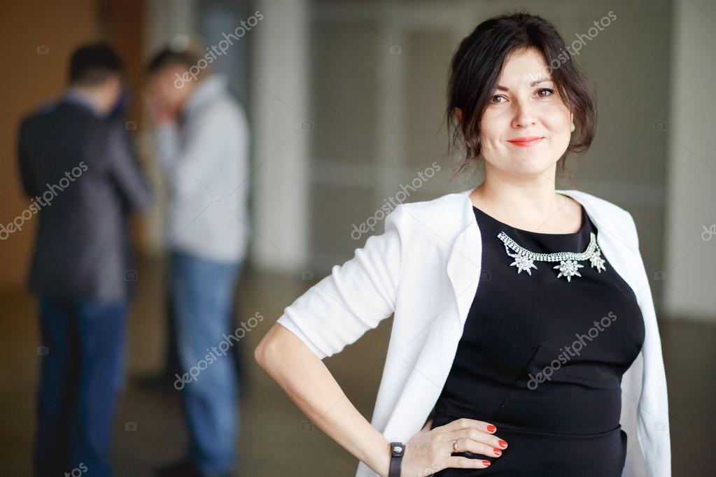 Successful attractive boss brunette with kind eyes stands inside office ...