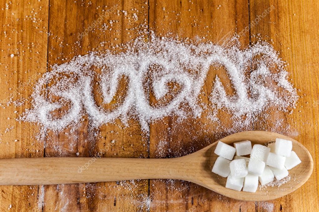 The word sugar written into a pile of white granulated sugar with spoon ...