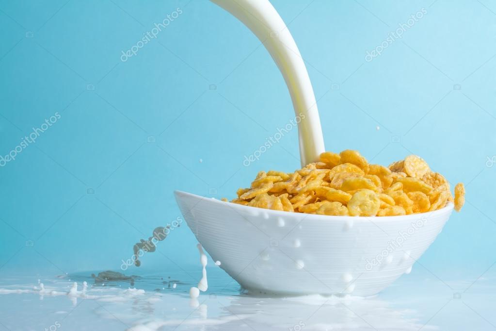 Milk stream pouring into a bowl with yellow flakes, milk splashes on a ...