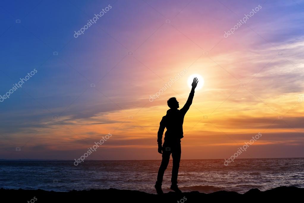 Happy man with hand up on sunset background, man on top of the mountain ...