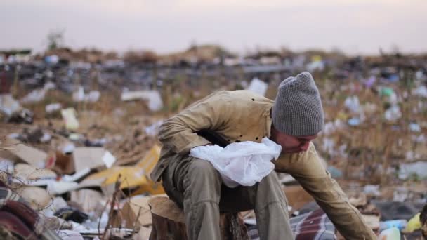Dirty homeless man sits on a close-up of the trash and eat the bread of ...
