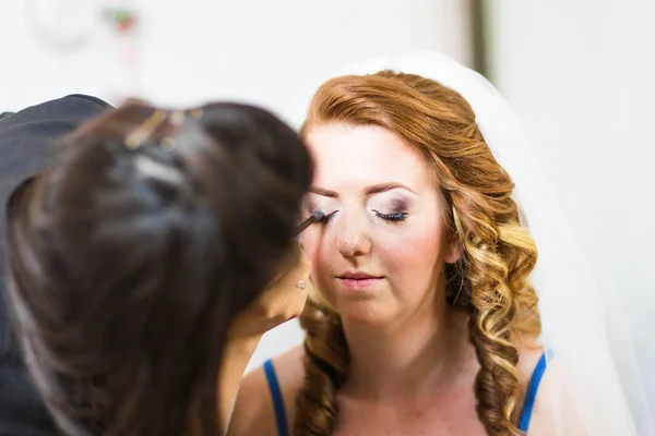 Young beautiful bride applying wedding make-up by make-up artist ...