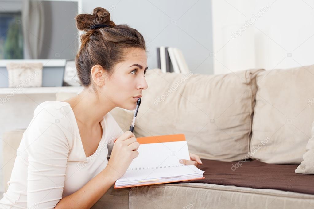 Mujer joven y bonita sentada en su acogedora cama y tomando notas de su diario, poco profundo de ...