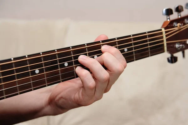A young man plays the guitar. He holds the strings with his fingers ...