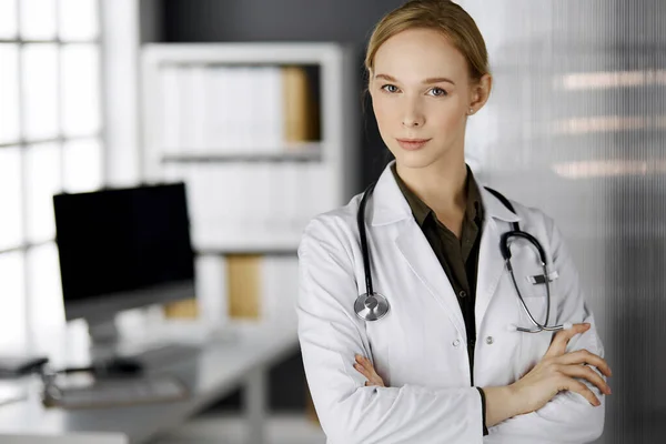 Friendly smiling female doctor standing in clinic. Portrait of friendly ...