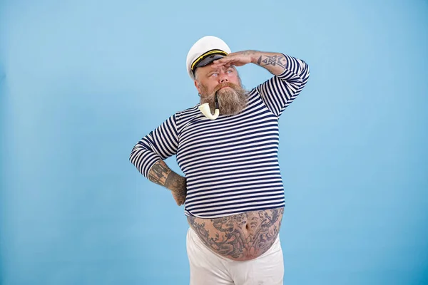 Dashing fat sailor with beard and smoking pipe holds foamy beer on ...