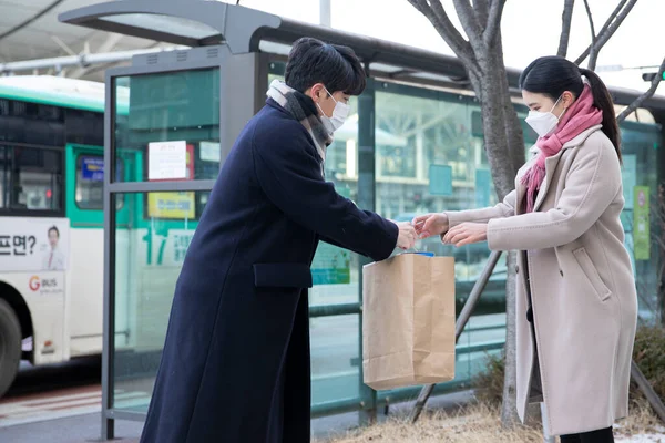Asian woman and man with face masks handing over paper bag, face to ...