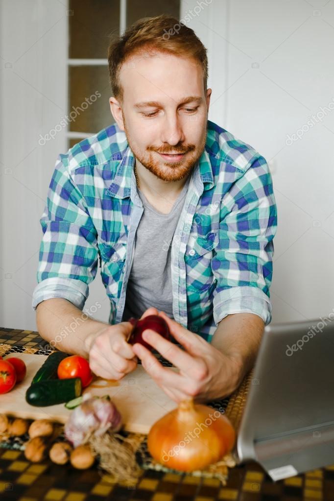 Young man cooking in home kitchen Stock Photo by ©ilya.oreshkov 95165536
