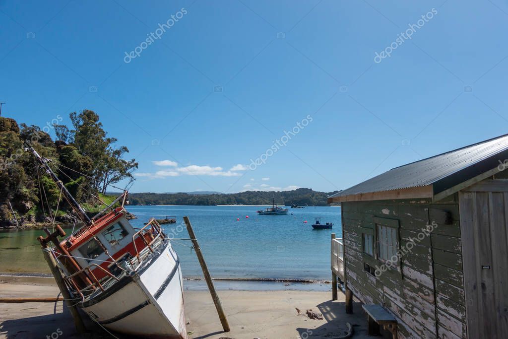 Leask Bay beach and boat sheds with beached old fishing boat lying it's ...