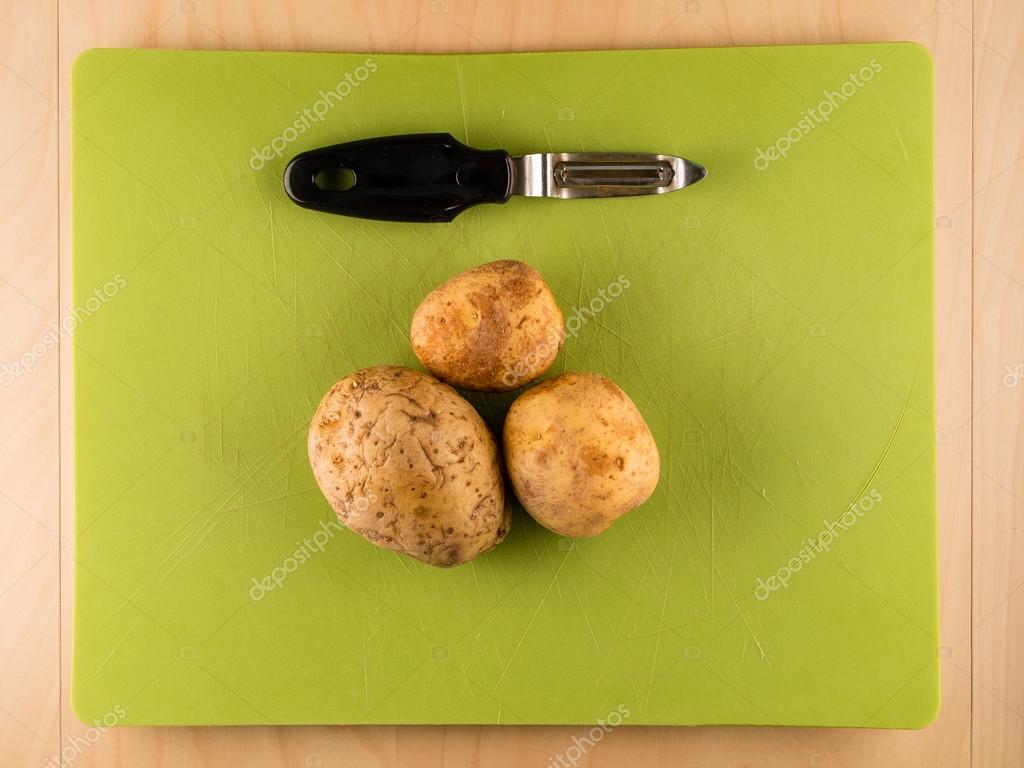 Tres patatas y pelador en tablero de plástico verde 2023