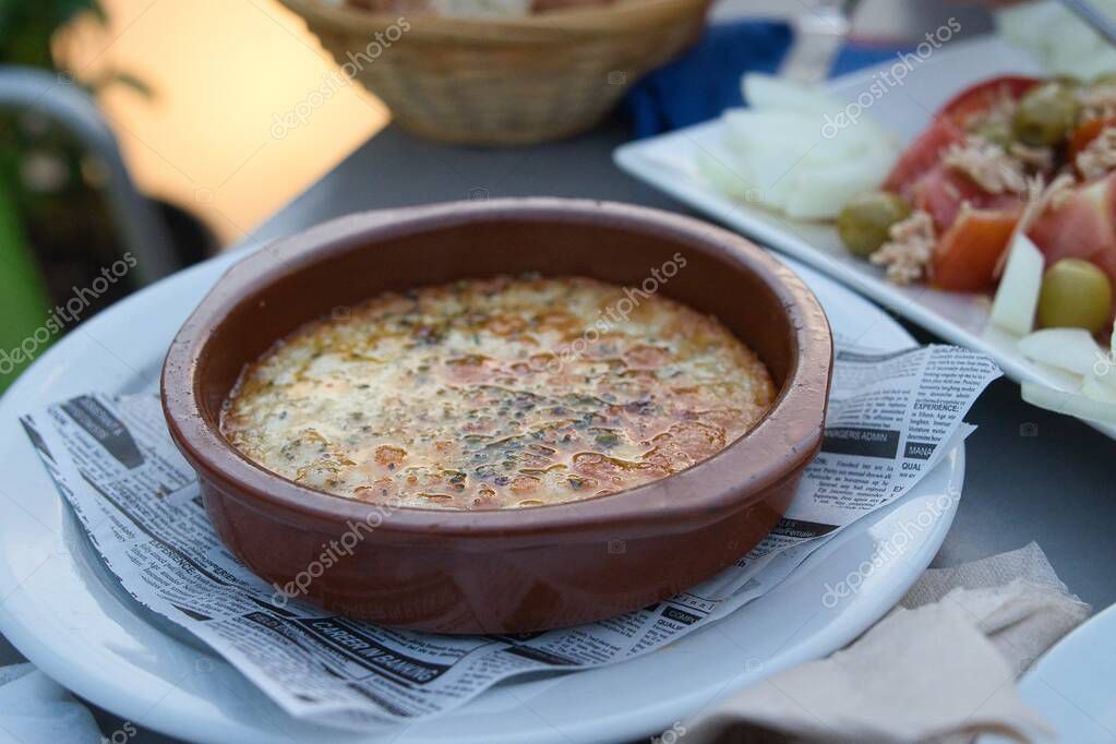 Queso Provolone en cazuela de cerámica roja en recorte de periódicos. 2023