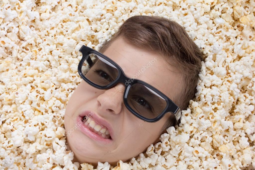 Evil ferocious young boy in stereo glasses looking out of popcorn ...