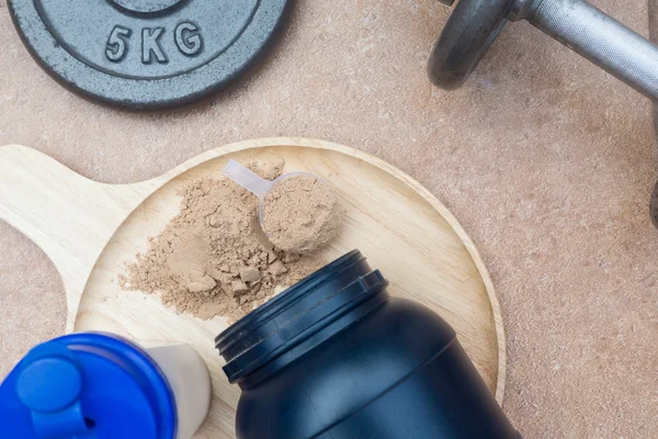 Whey protein powder in scoop with vitamins on plate on wooden ...