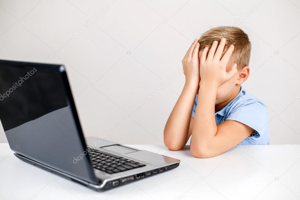Scared kid covering his face at desk with laptop Stock Photo by ...