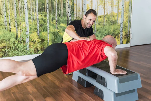 Personal trainer helping a man do push-ups indoors - Stock Image ...