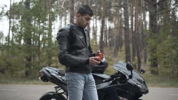 Side view of sad young Middle Eastern man standing at motorcycle and ...